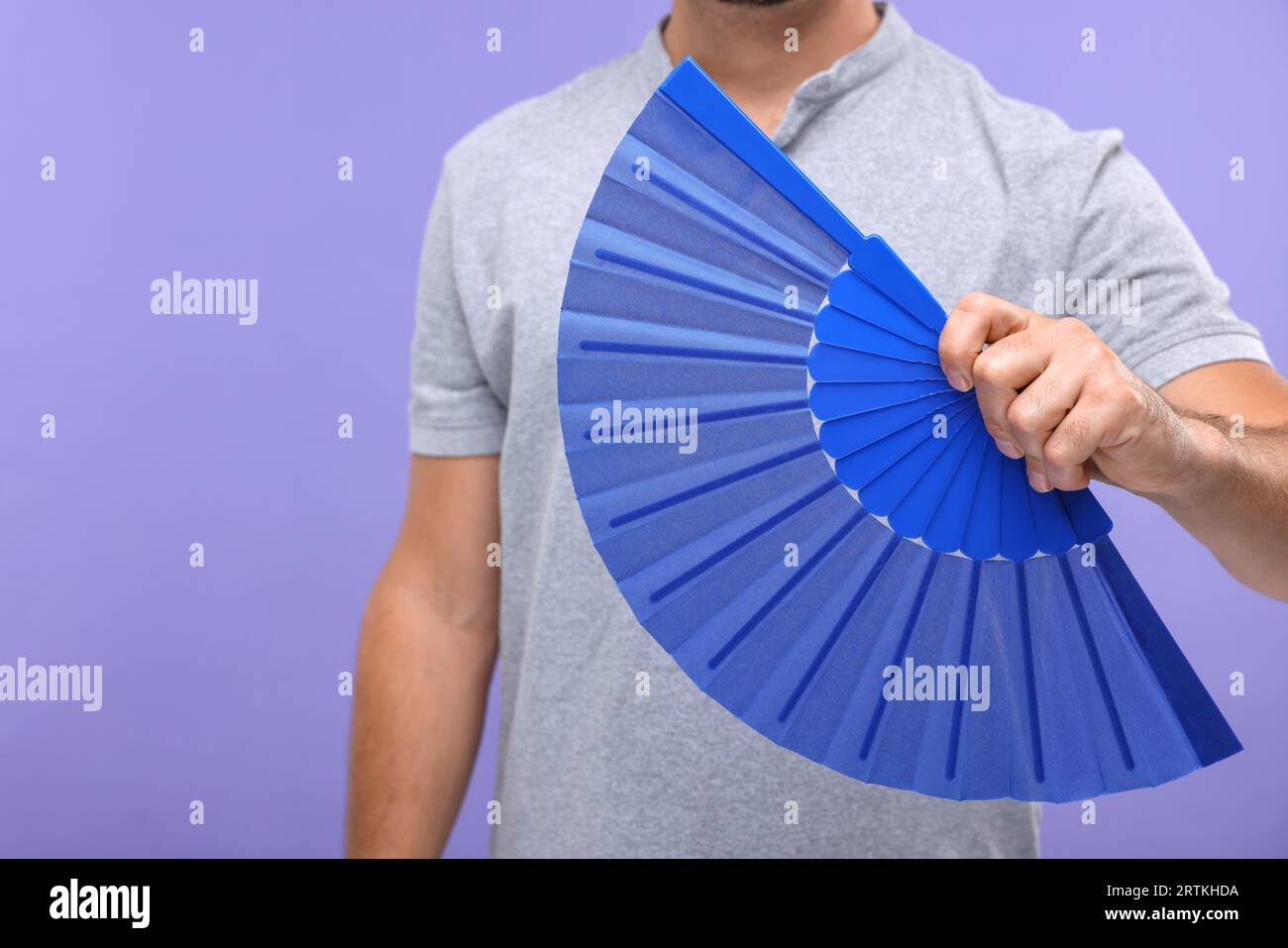Man holding hand fan on purple background, closeup. Space for text ...