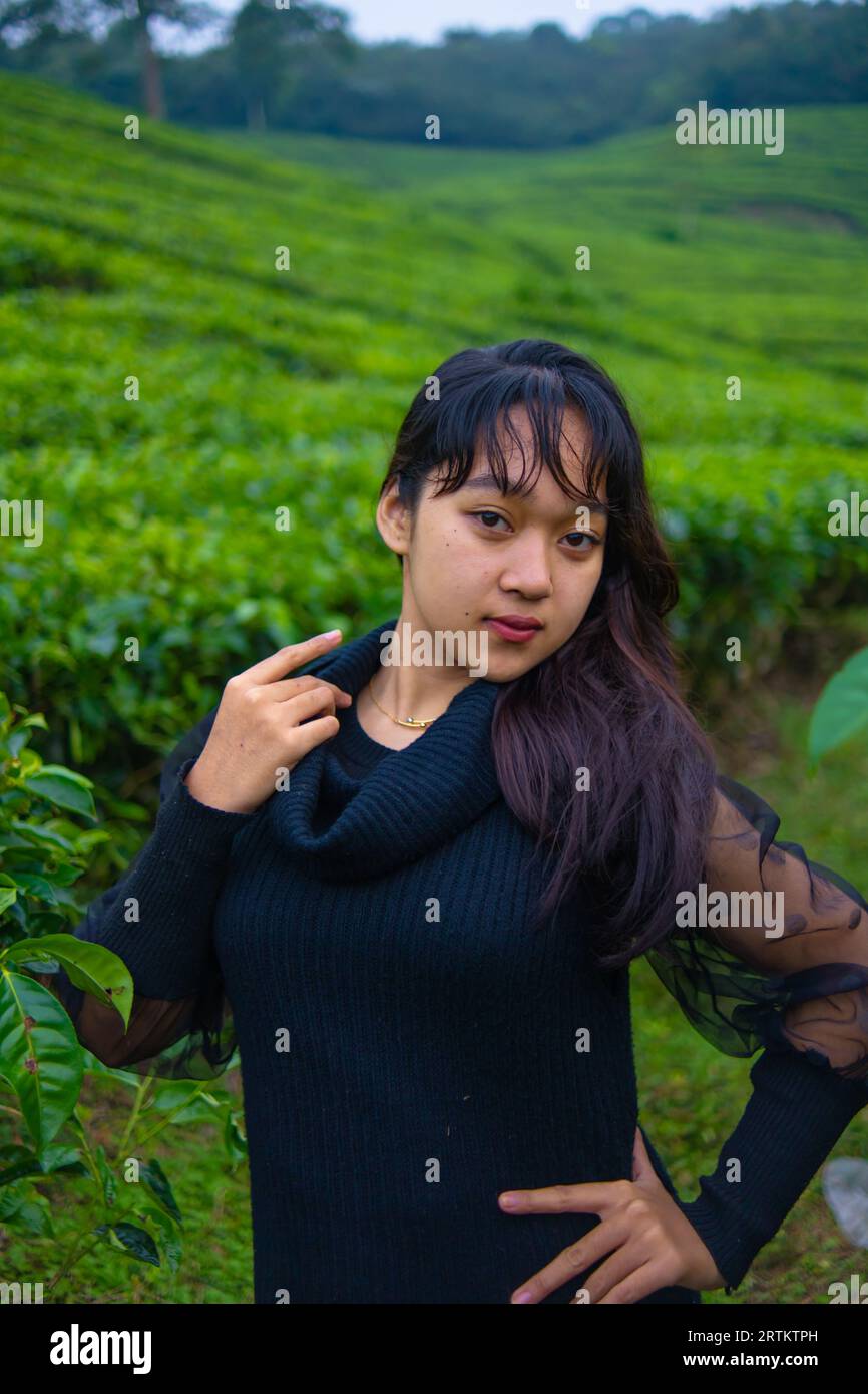 an Asian woman in a black dress is posing in front of a very beautiful tea plantation in the ...