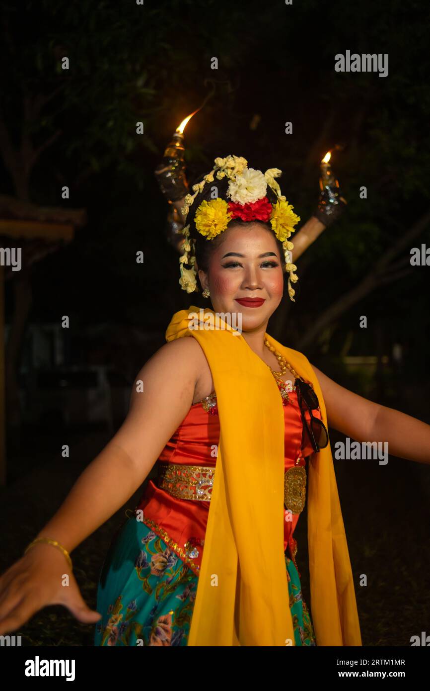 a traditional Javanese dancer dances with colorful flowers on her fist ...