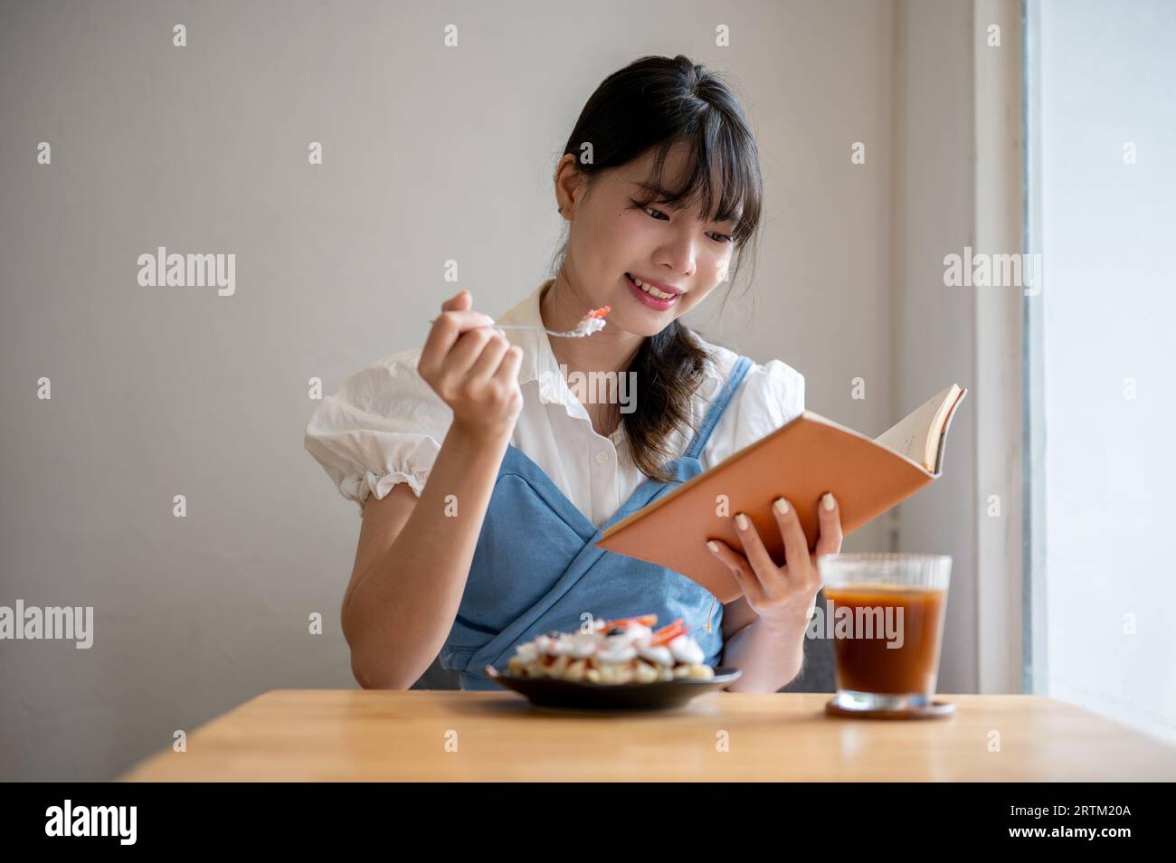 A charming and happy young Asian woman enjoys reading a book while ...