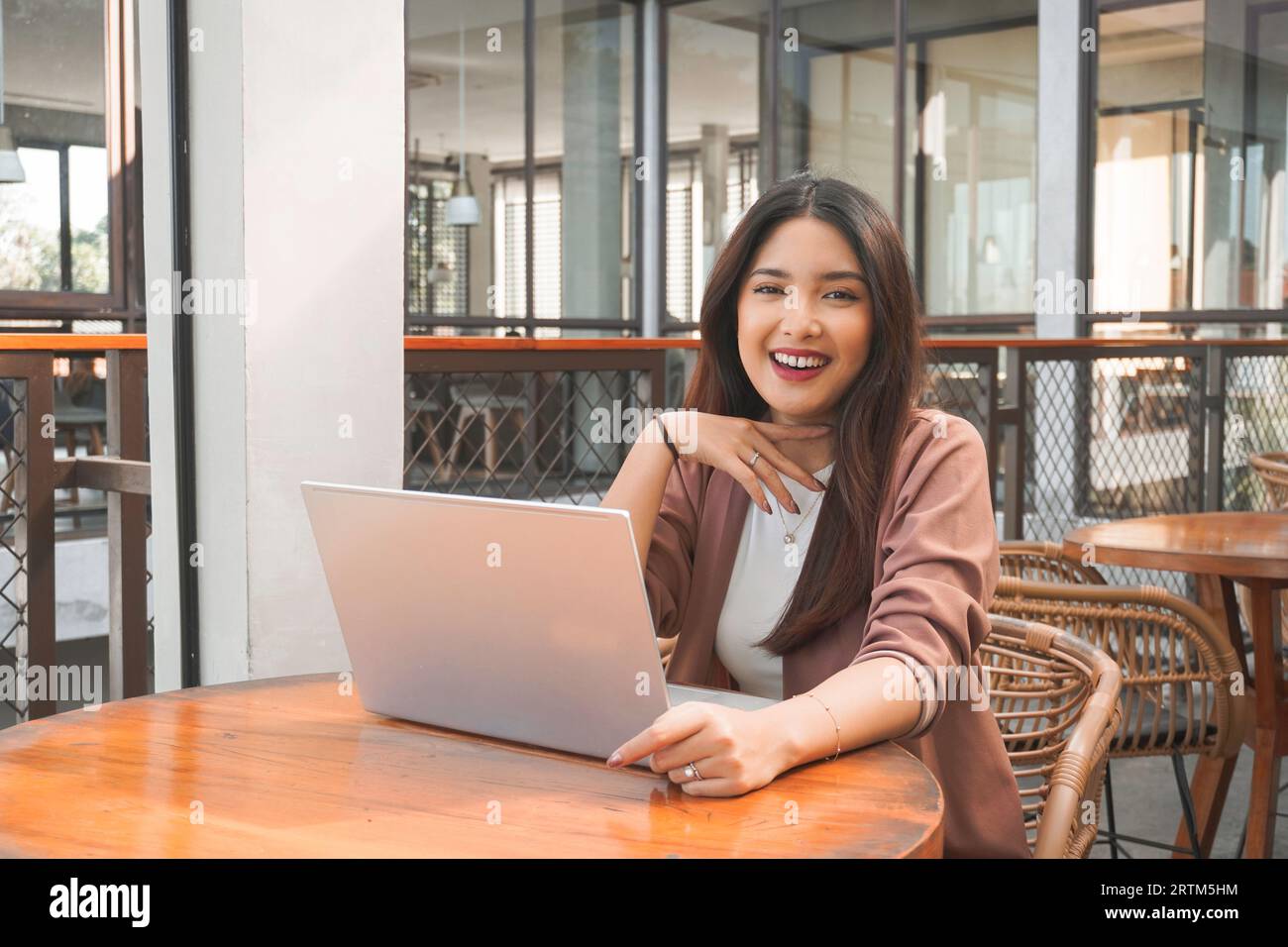 Smiling young Asian woman working remotely from cafe using her laptop ...