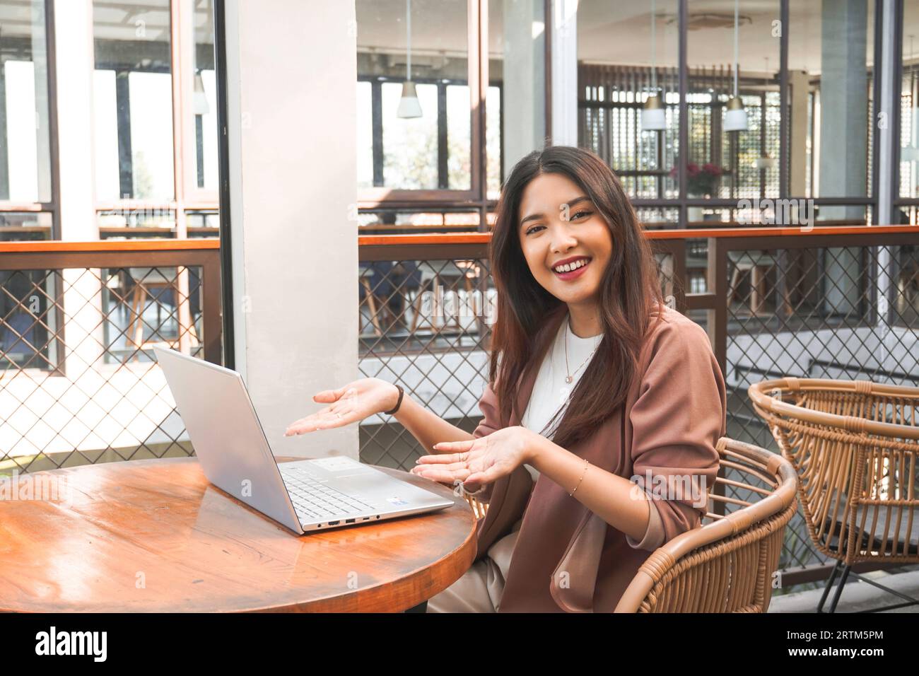 Smiling young Asian woman working remotely from cafe using her laptop ...