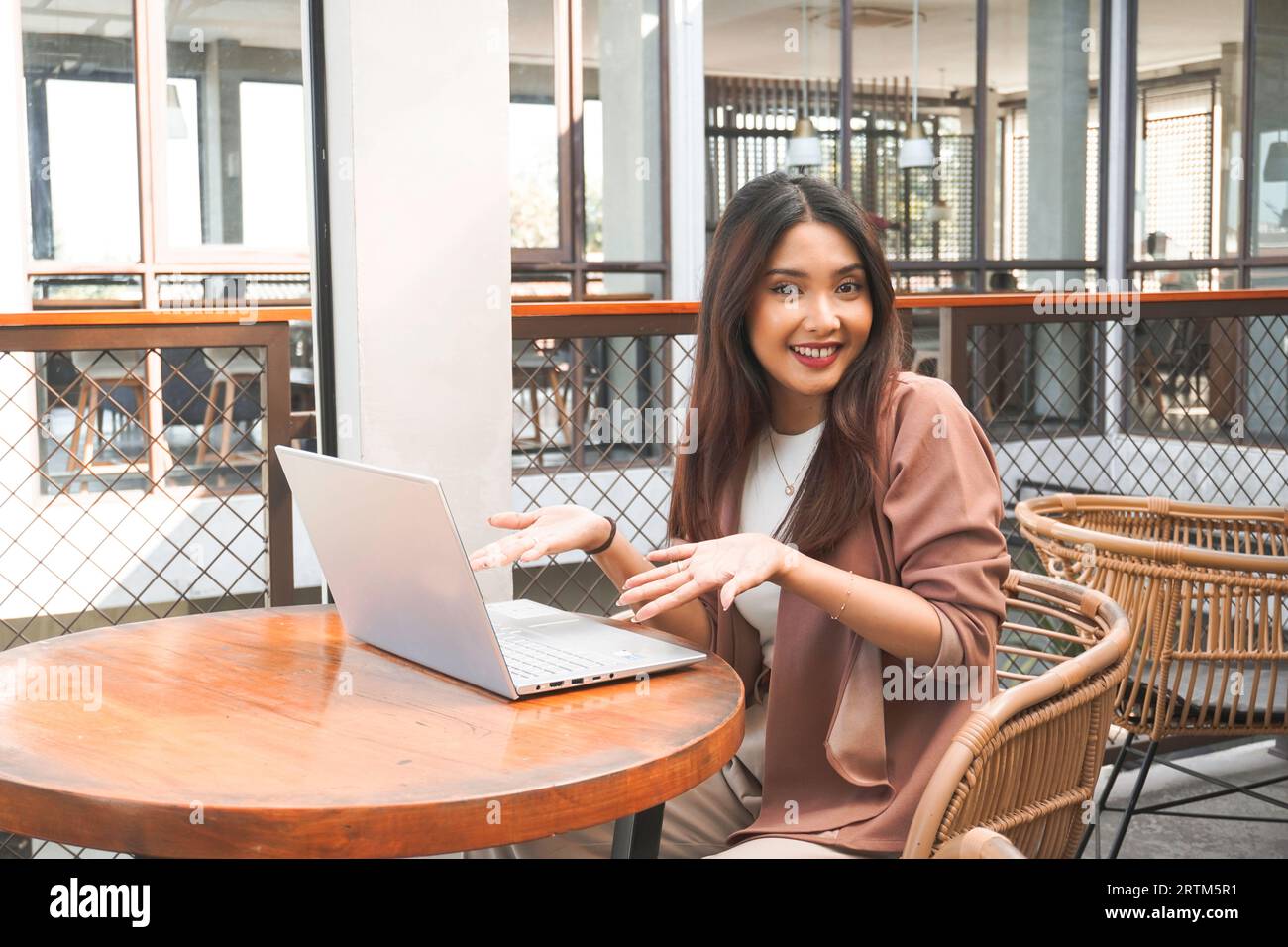 Smiling young Asian woman working remotely from cafe using her laptop ...