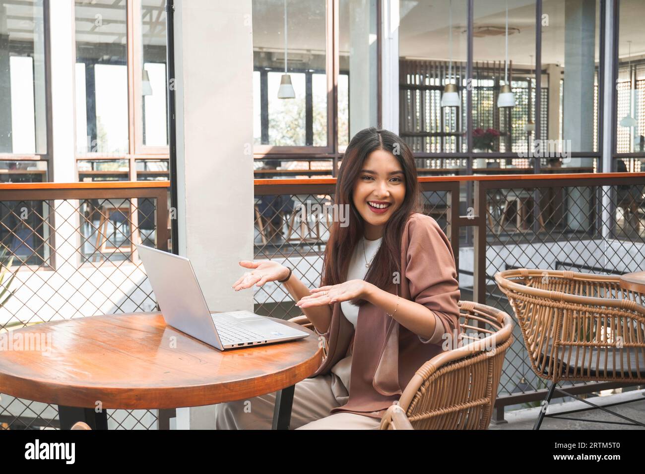 Smiling young Asian woman working remotely from cafe using her laptop ...