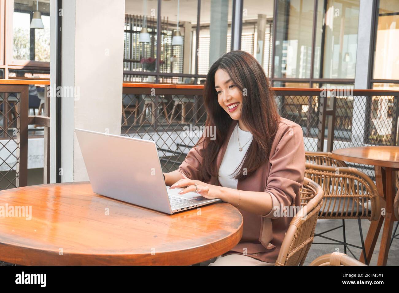 Smiling young Asian woman working remotely from cafe using her laptop ...
