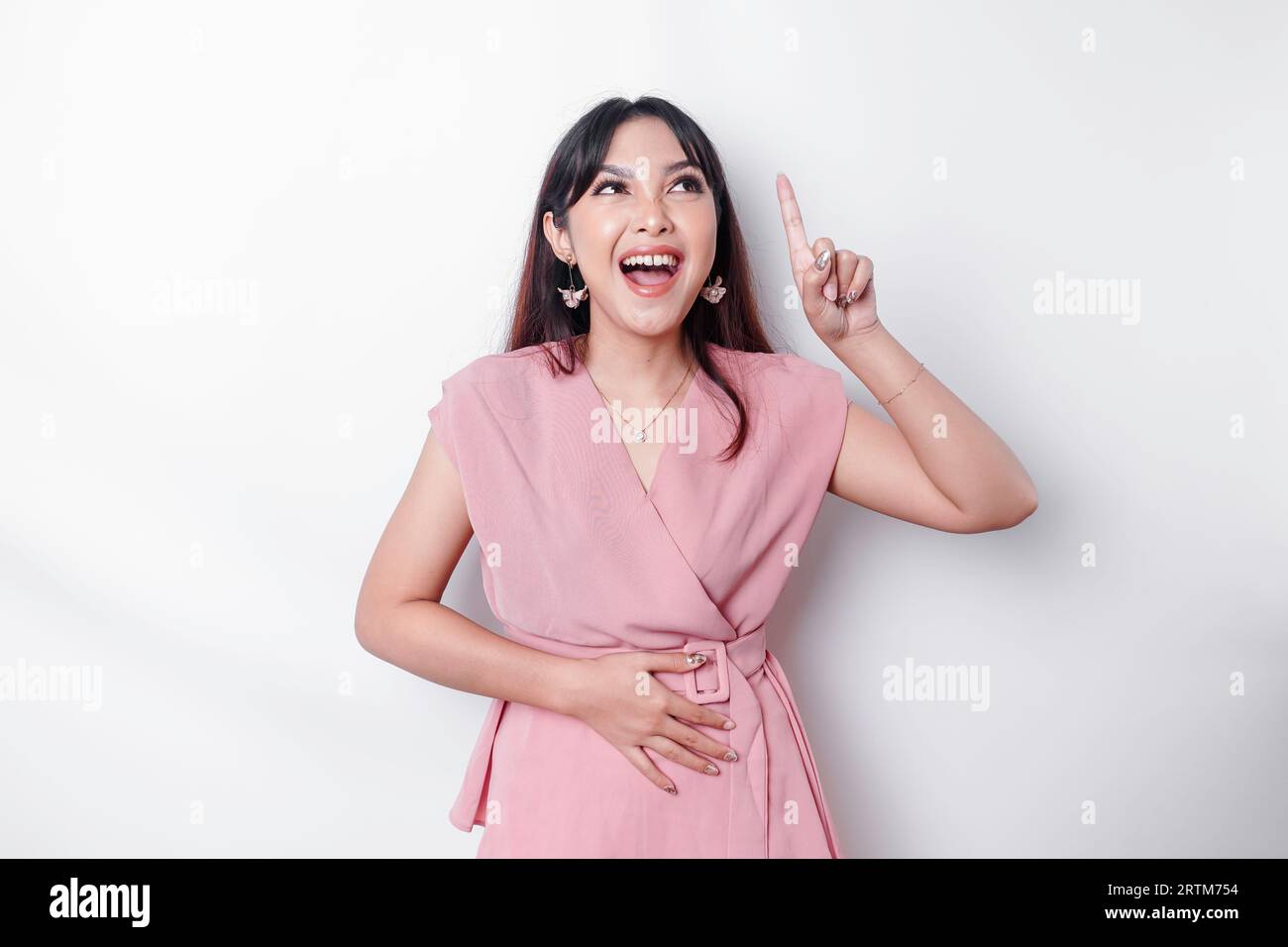 Starving Asian woman dressed in pink, pointing at the copy space on top ...