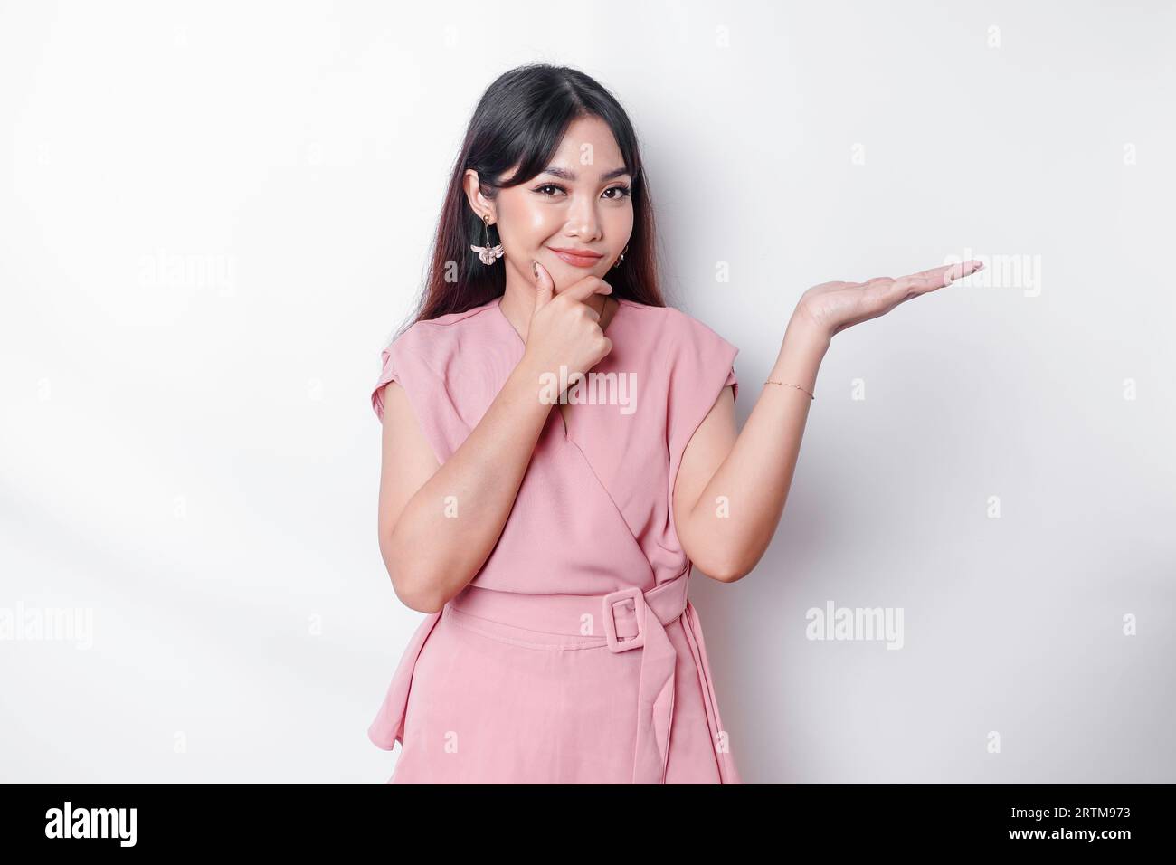 A thoughtful young woman dressed in pink and holding her chin while ...