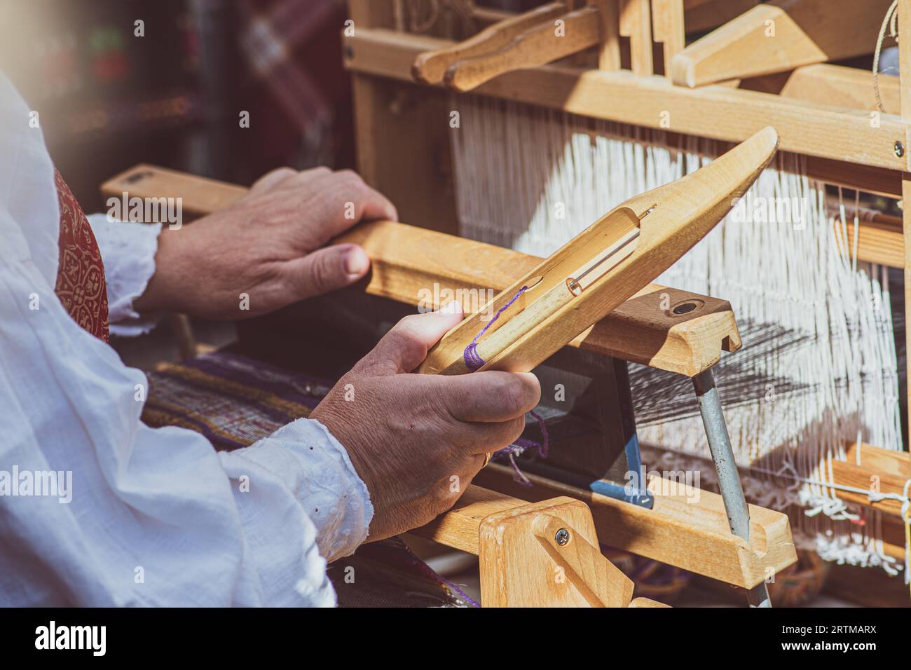 A craftswoman working on an ancient wooden weaving loom in traditional ...