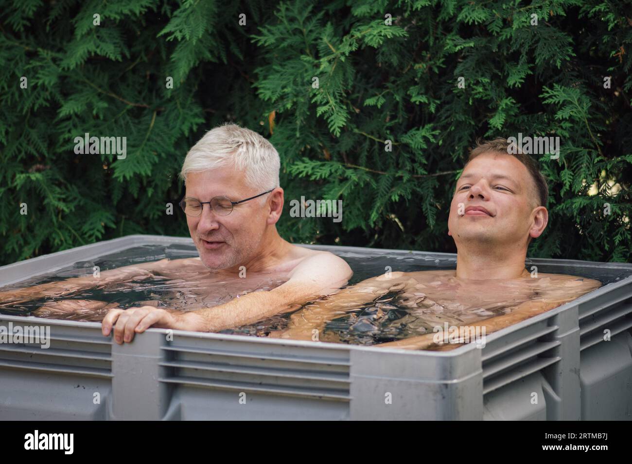 Couple of male friends ice bathing in the cold water among ice cubes ...