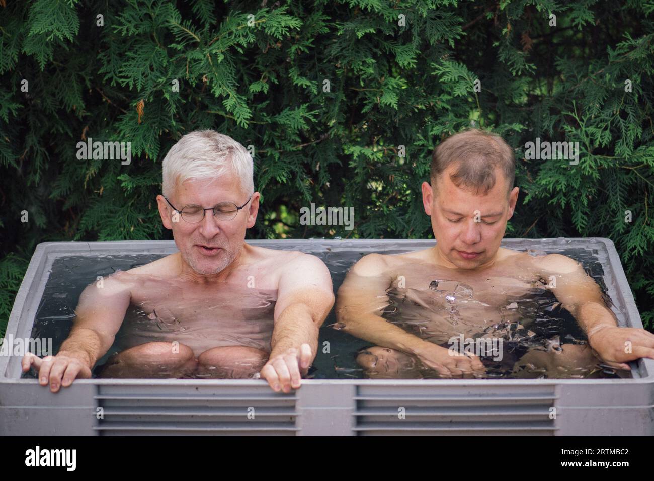 Couple of male friends ice bathing in the cold water among ice cubes ...