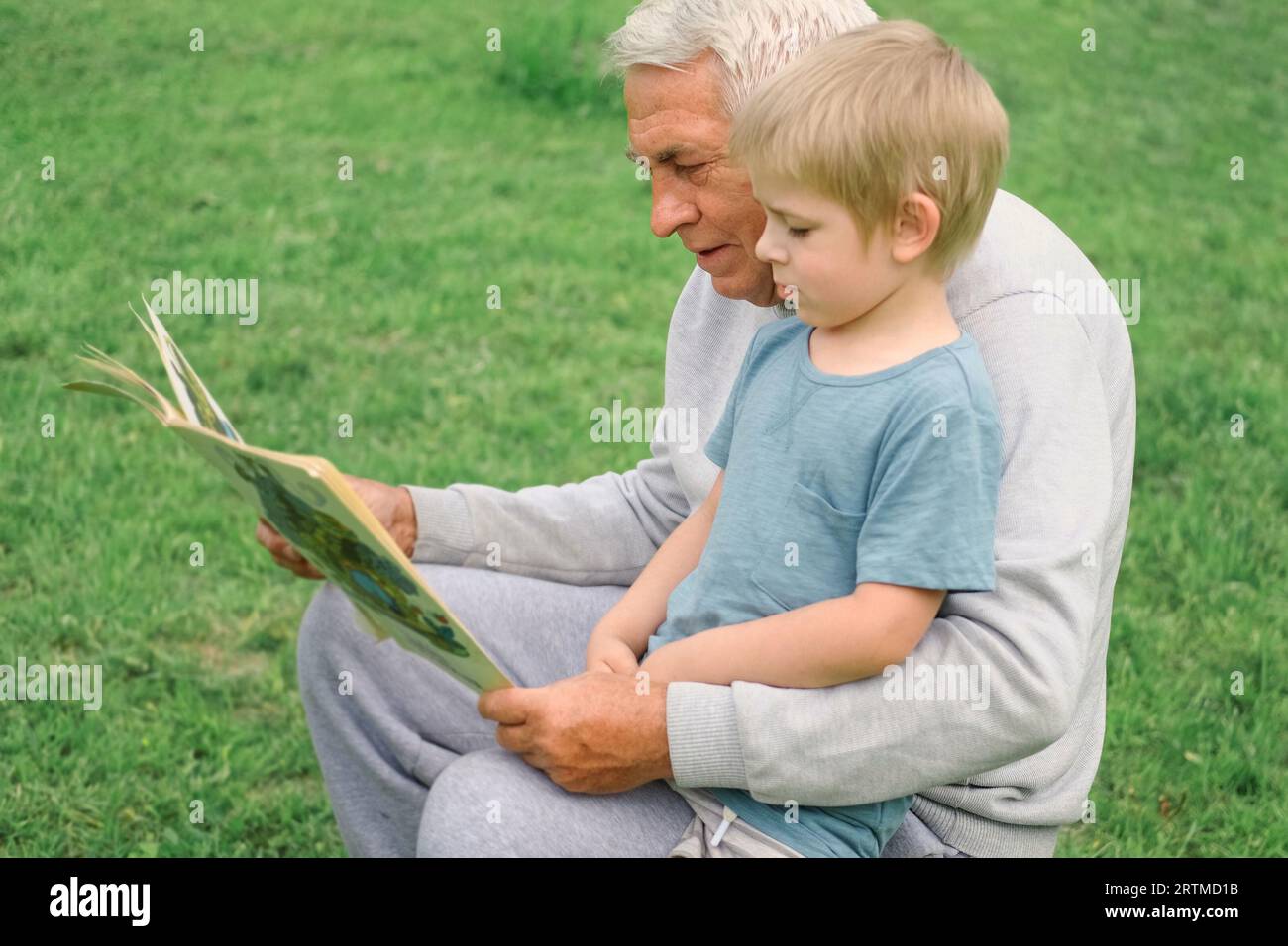 Happy grandfather reading book to curious grandson outdoors. Close up ...