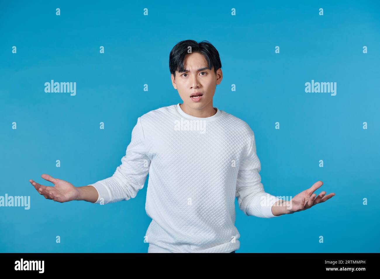 Sad and confused asian man standing with open hands. Isolated on blue ...