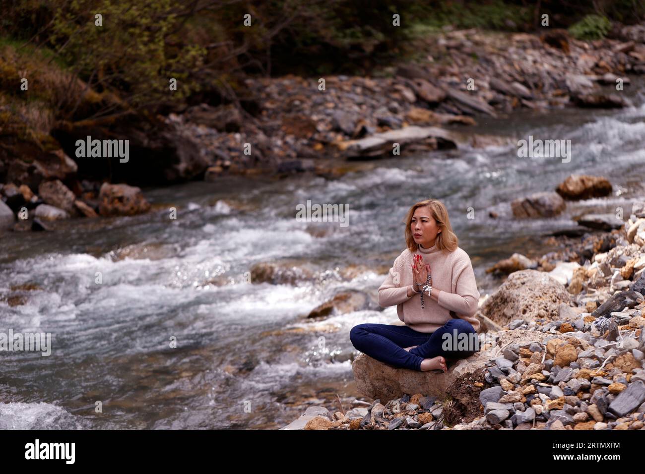 Praying woman sitting on a rock at the edge of a river. Concept of ...