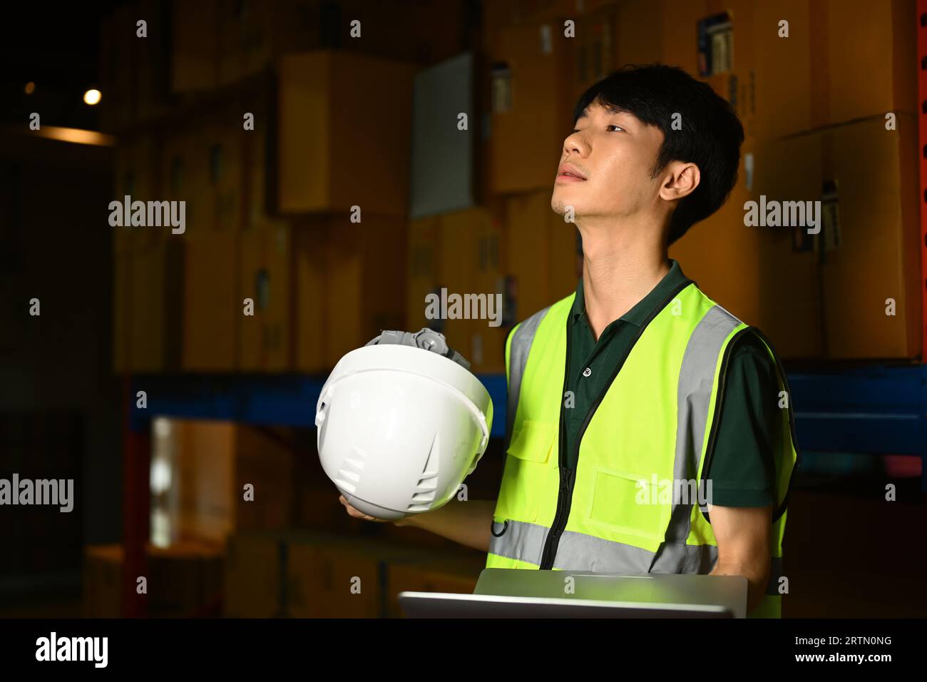 Tired male worker leaning shelves and taking break from hard work in large retail warehouse ...
