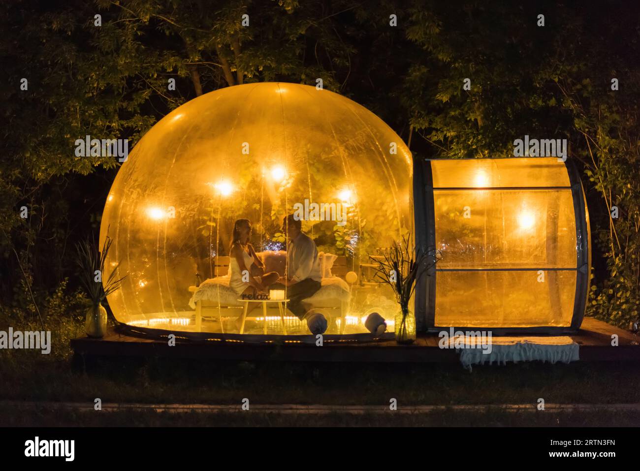 A couple sitting inside transparent bubble tent with illumination at ...