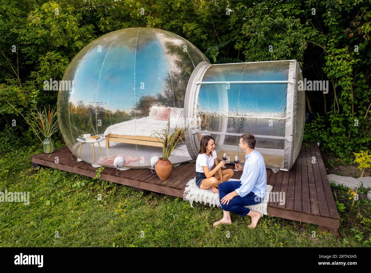 A happy couple drinking wine near transparent bubble tent at glamping ...