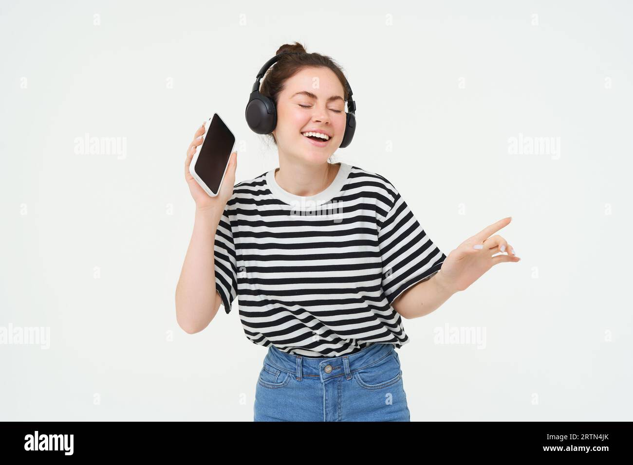 Girl with smartphone dancing, listening to music in wireless headphones ...