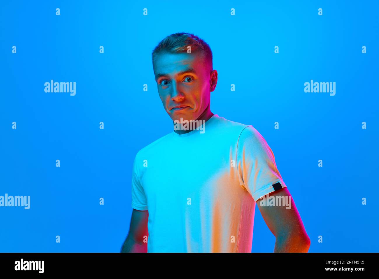 Wow. Young man's portrait on blue studio background in neon light ...