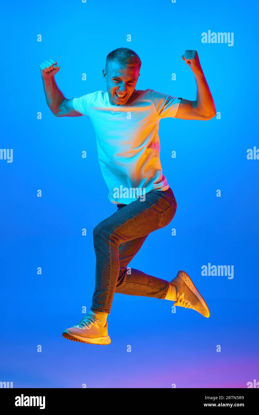 Neon light portrait of victorious delighted happy, jumping man raising ...
