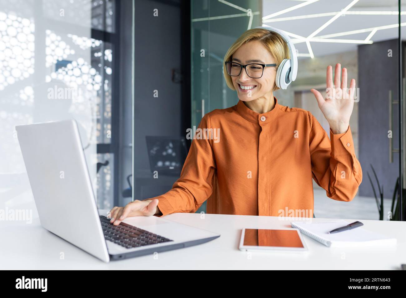 Young joyful woman at workplace listens to music in headphones ...