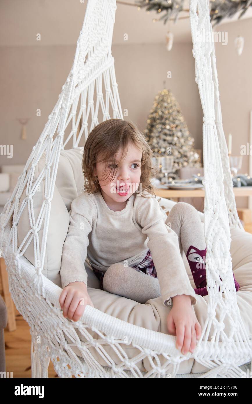 Close-up portrait of a funny little girl on a wicker macrame swing near ...