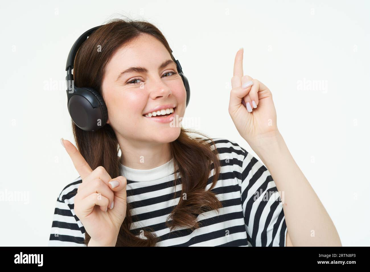 Dancing girl in wireless headphones pointing at empty space for music ...