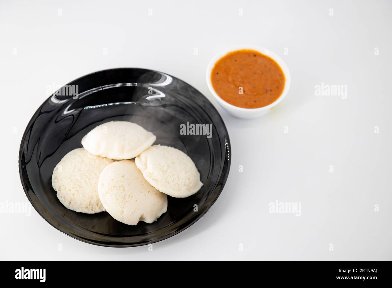Hot and steaming idly in a black plate and tomato chutney in a isolated ...