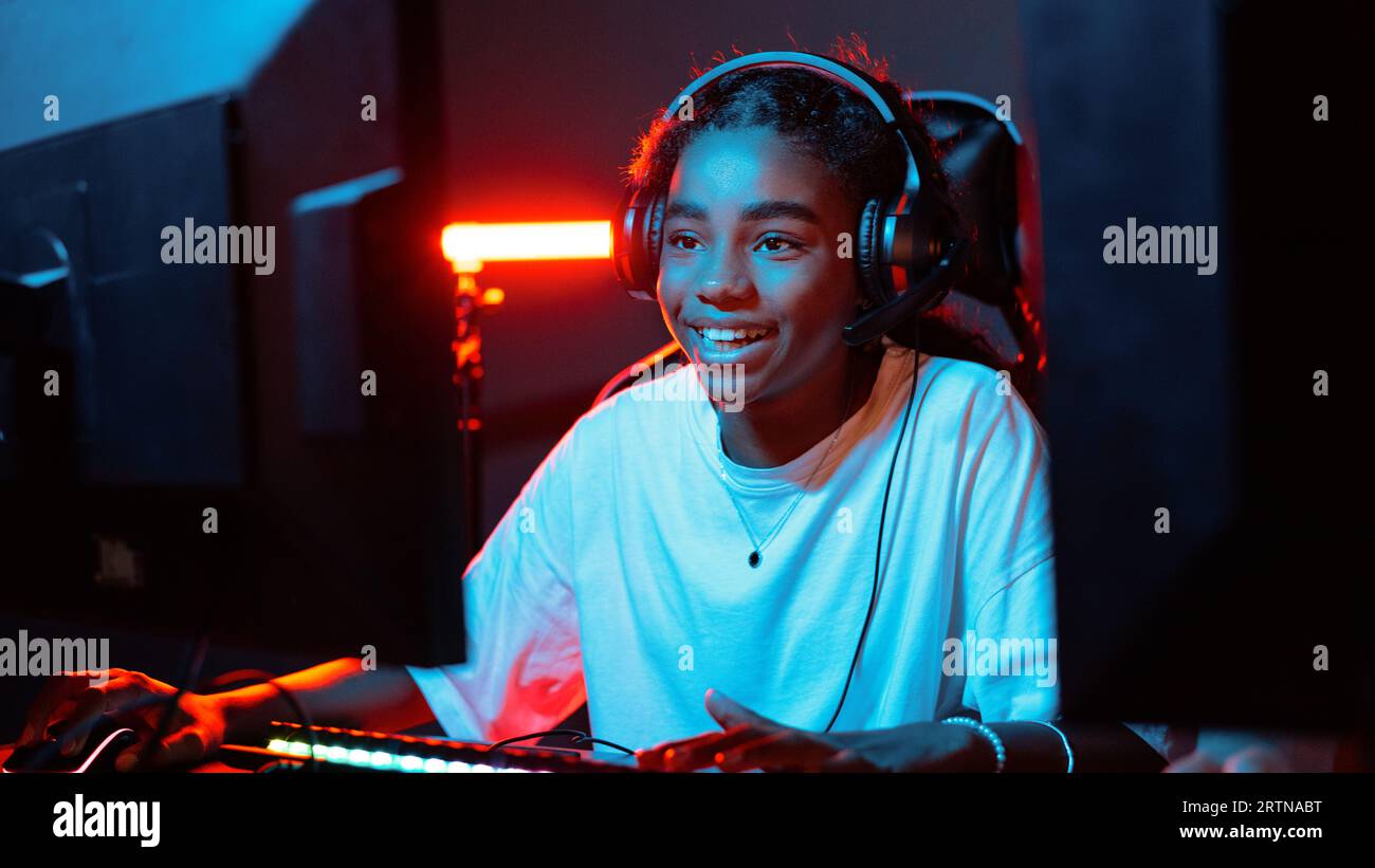 Black teen smiling girl in headset playing video games in video game ...