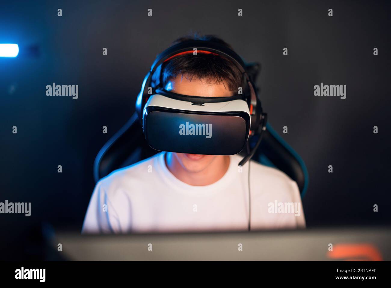 Teen boy in VR headset playing video games in video game club with blue ...