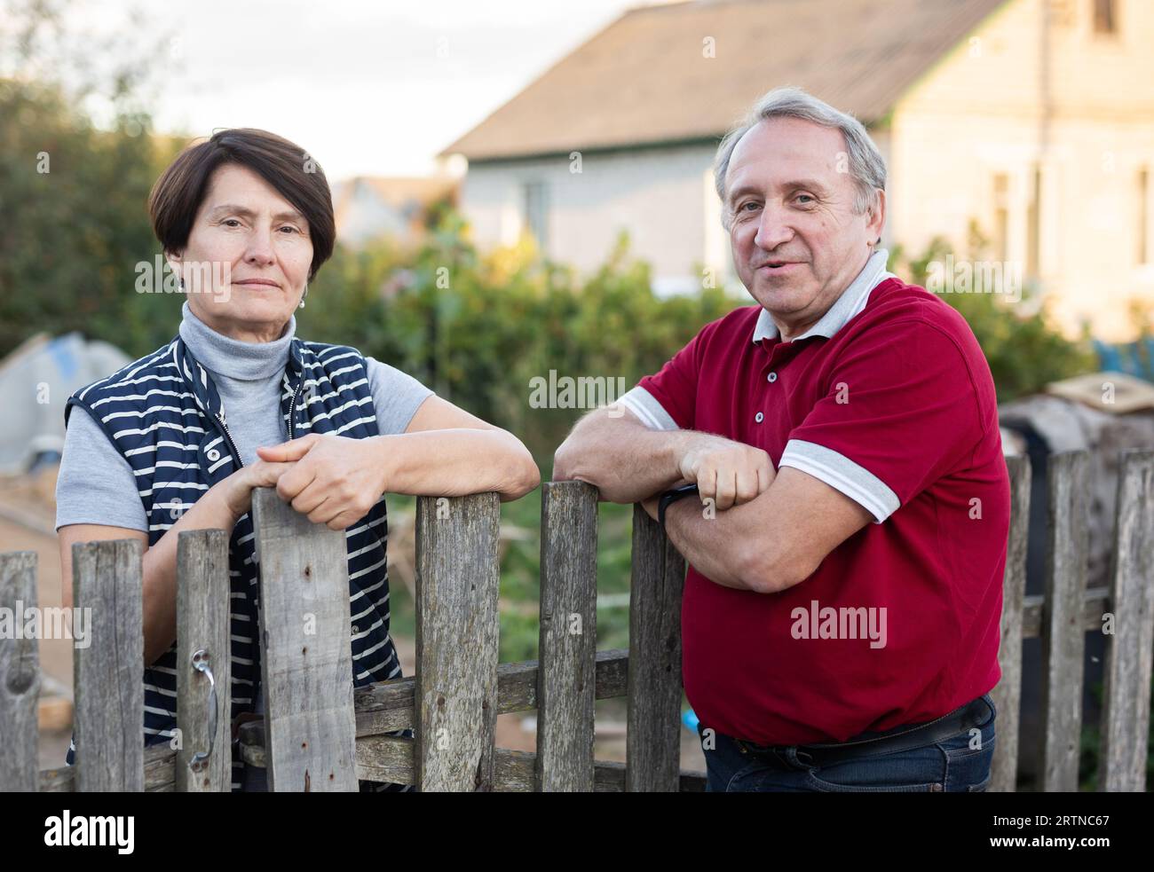 Neighbors standing at fence outdoors and having conversation. Village ...