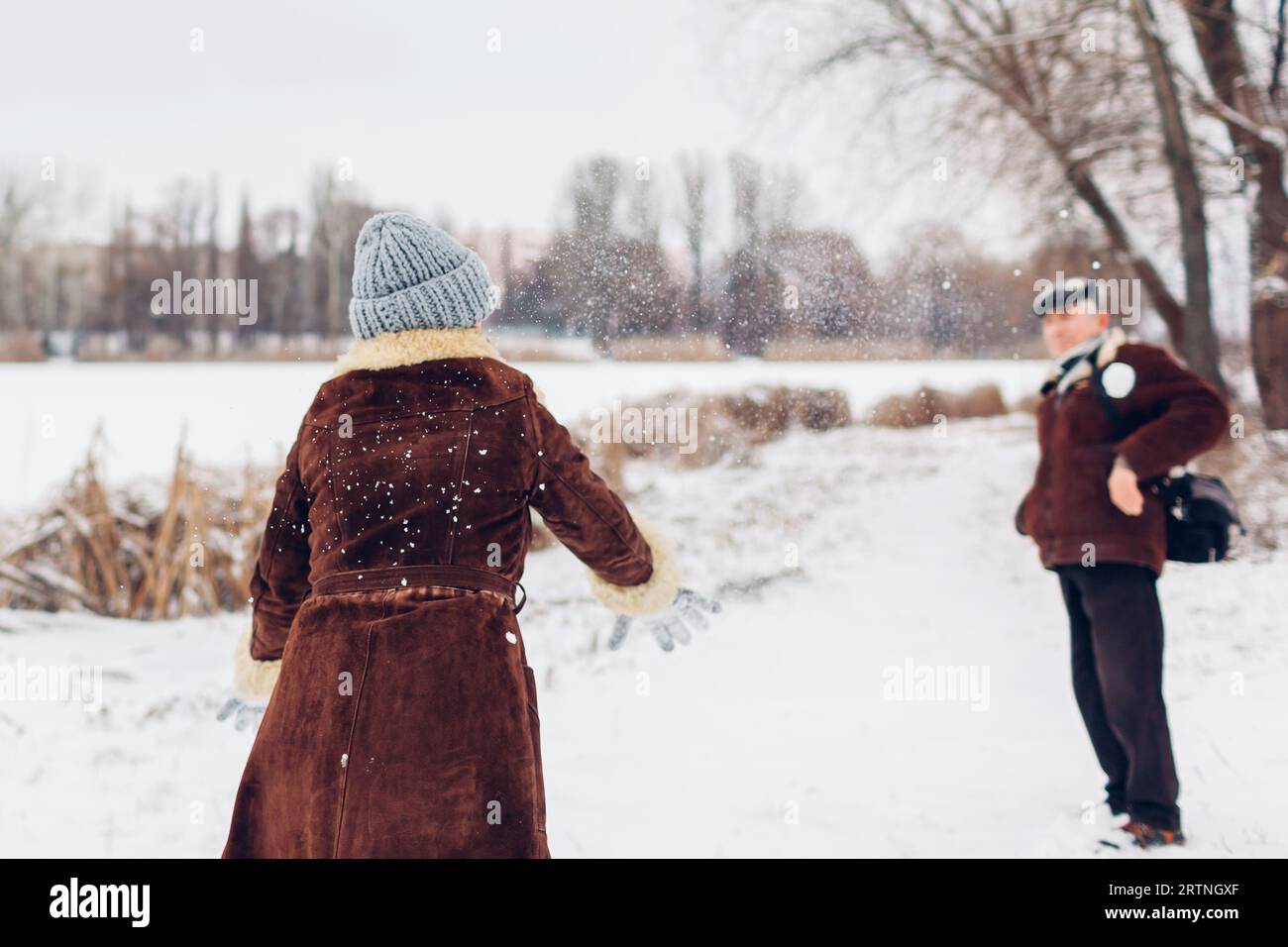 Senior family couple playing snowballs outdoors during snowy winter ...