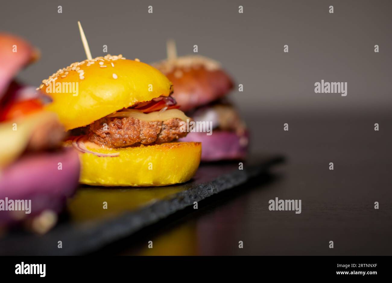 Colored Mini Gourmet Burgers with sesame seeds on black slate board ...