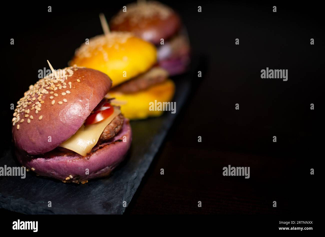 Colored Mini Gourmet Burgers with sesame seeds on black slate board ...