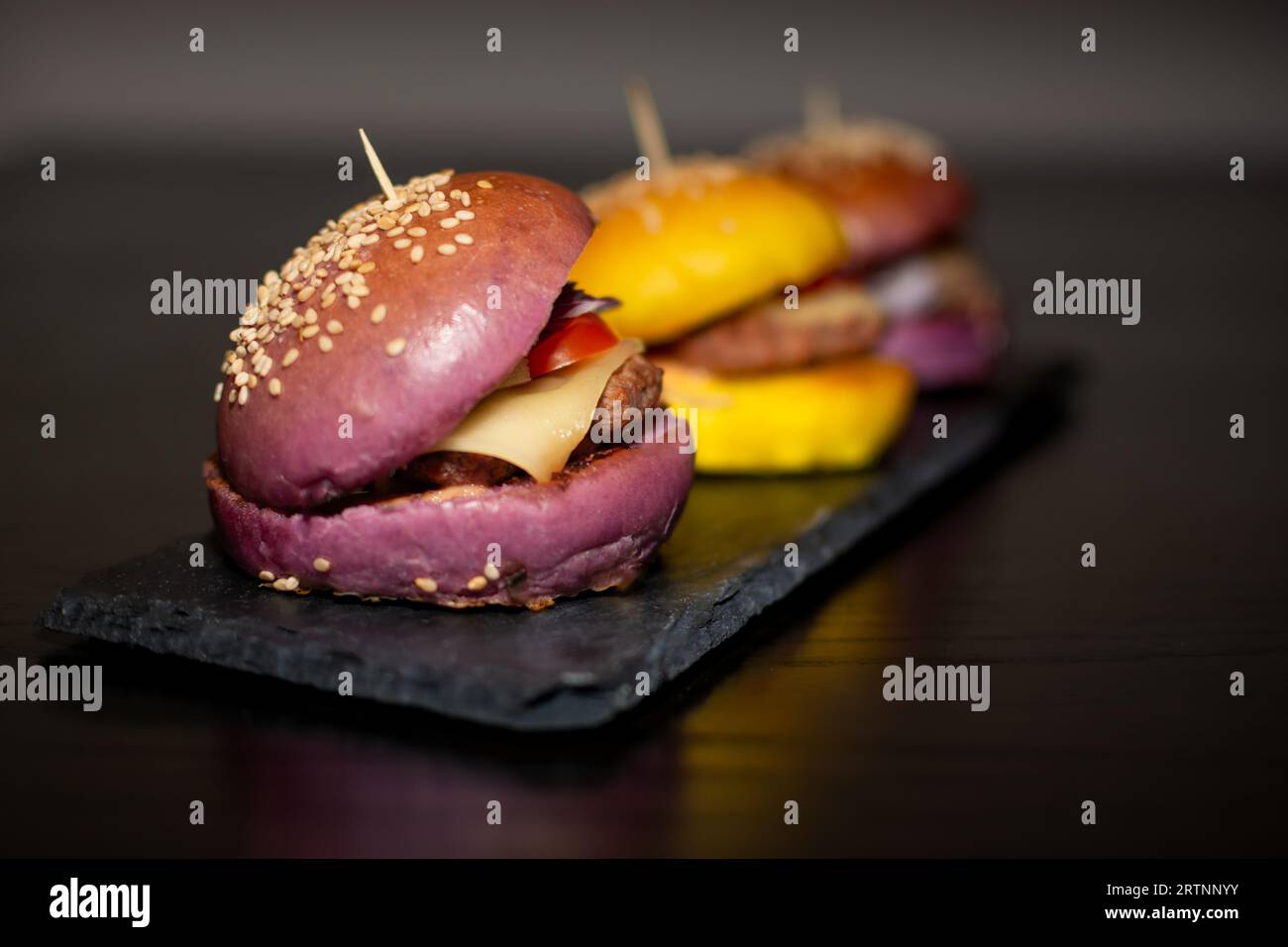 Colored Mini Gourmet Burgers with sesame seeds on black slate board ...