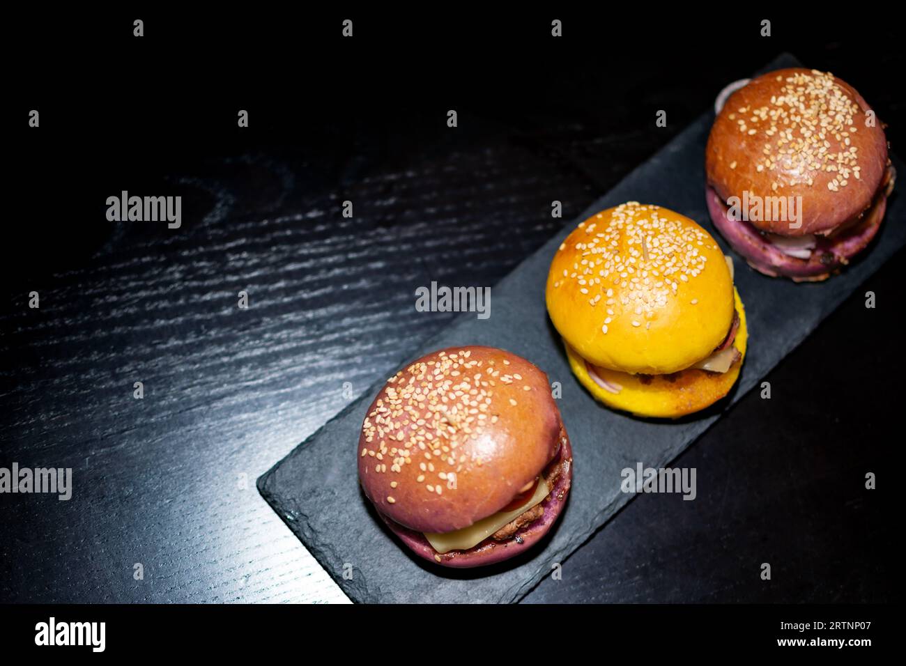 Colored Mini Gourmet Burgers with sesame seeds on black slate board ...