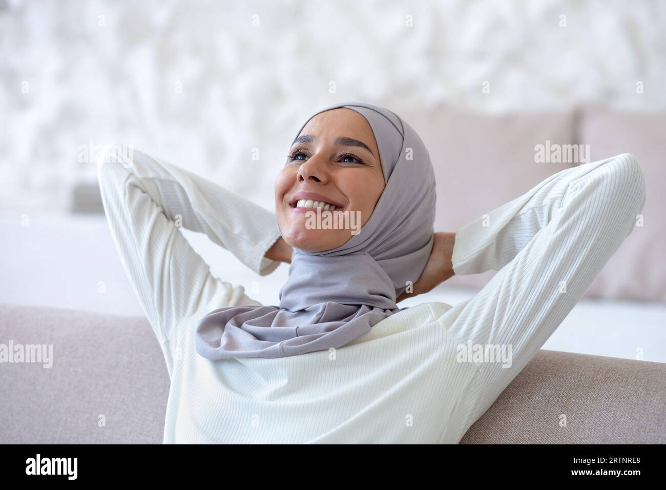 Happy young muslim woman in hijab sitting relaxed on sofa at home and ...