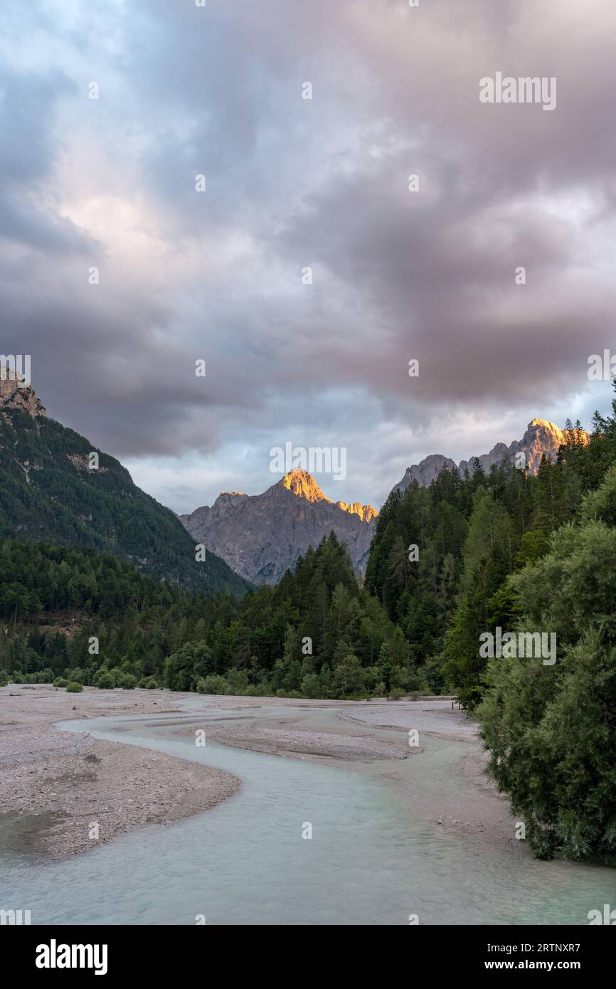 The setting sun hitting the peak of the mountain above a glacial, blue ...
