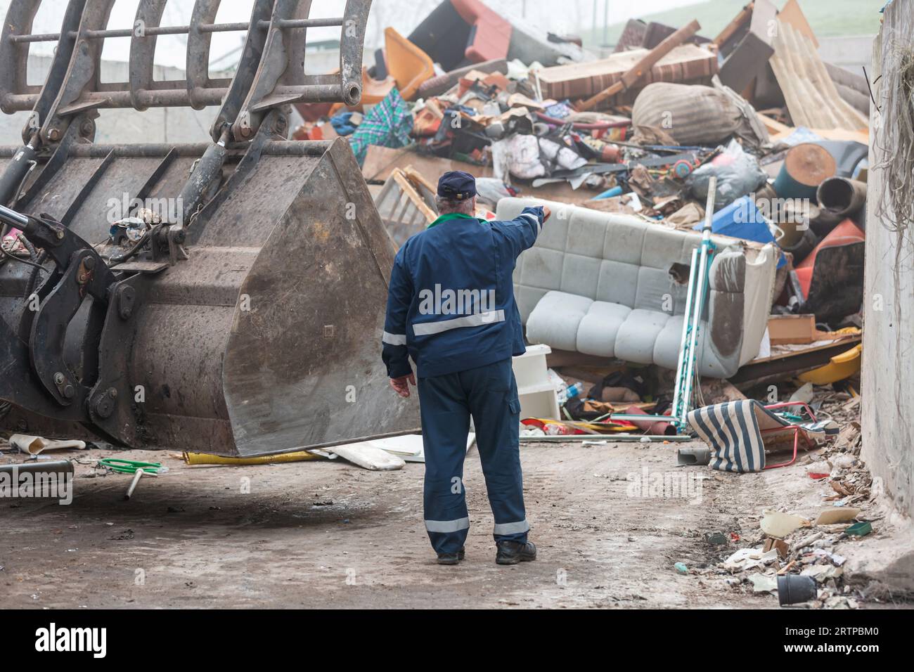 Male worker pointing on wheel loader and the garbage heap at a landfill ...