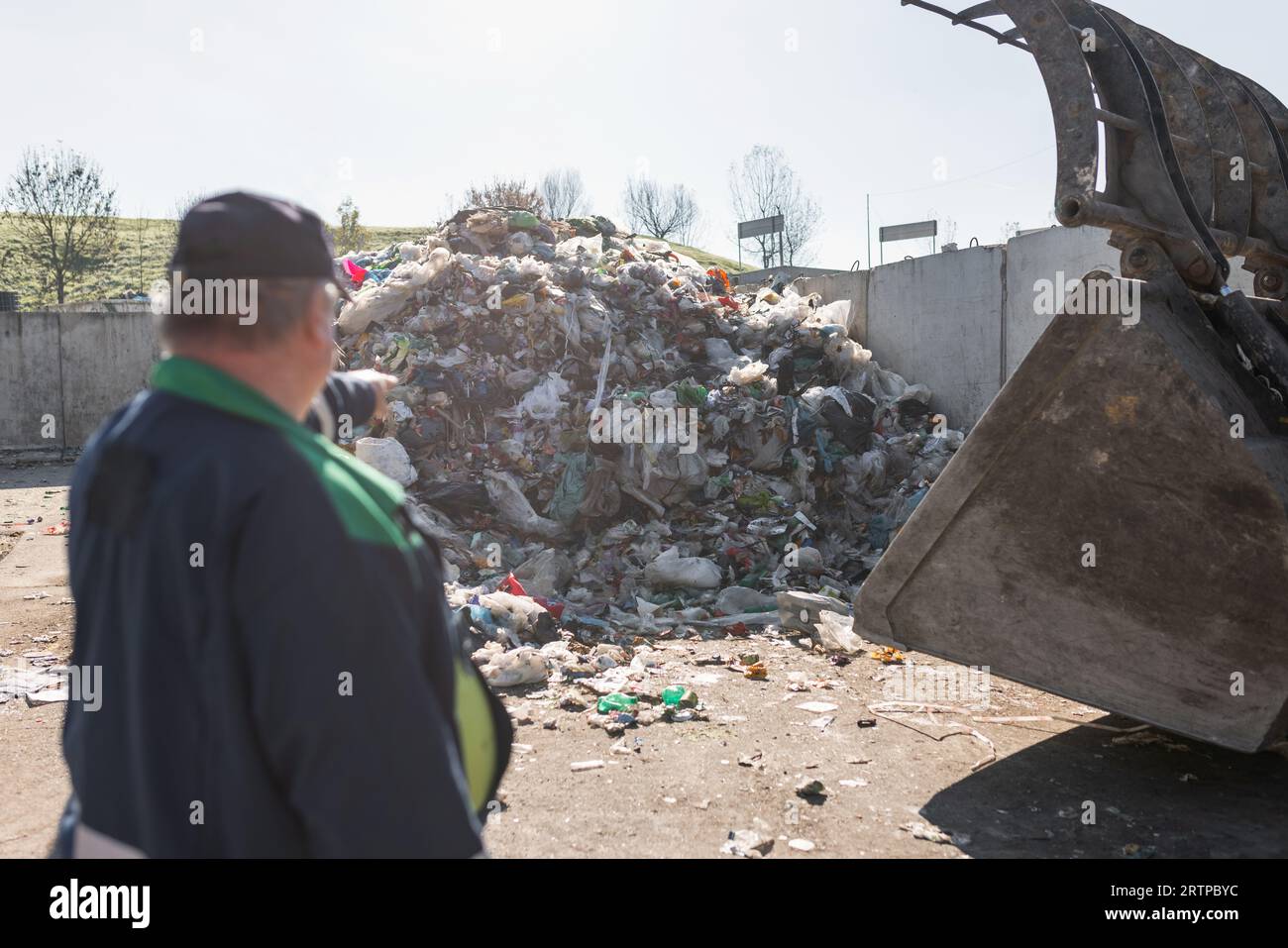 Landfill worker directing skid steer loader on the garbage heap. Waste ...