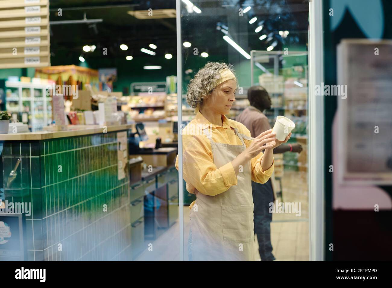Manager in uniform controlling the shelf life of goods in supermarket ...