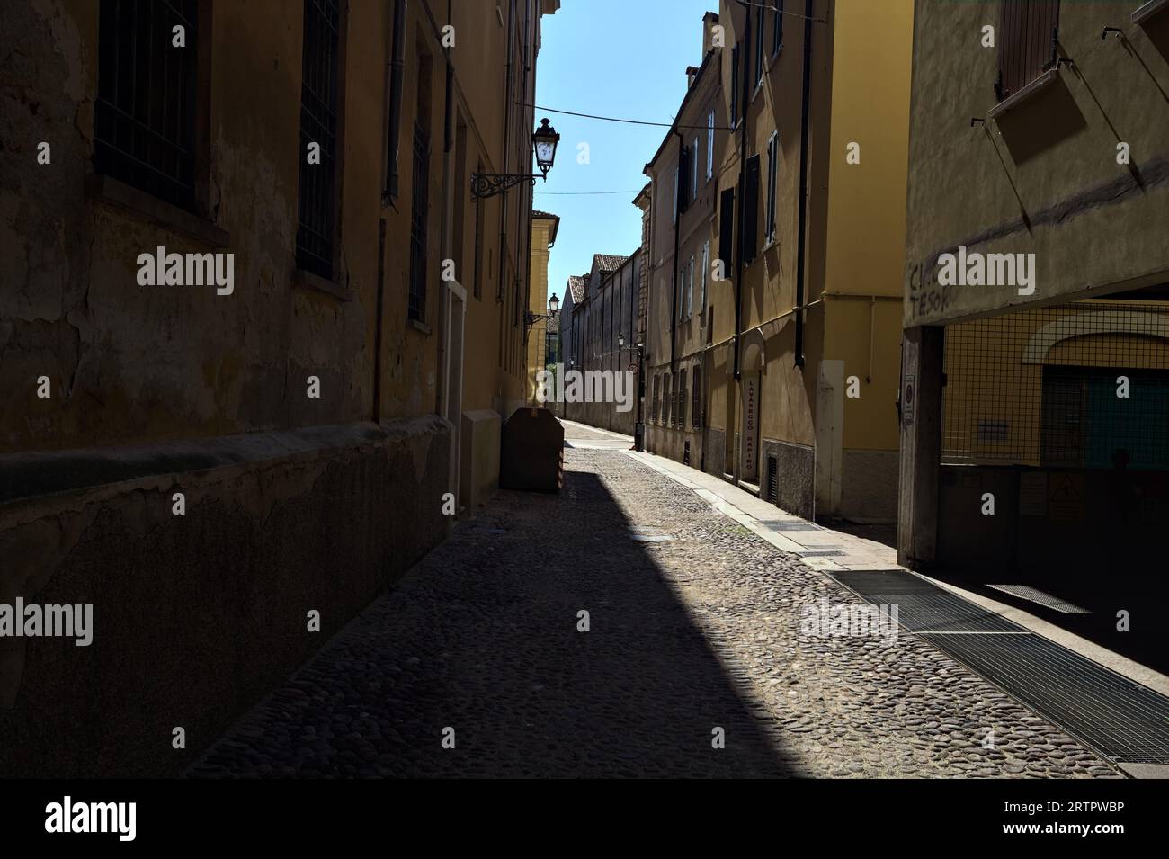 Narrow cobbled alley partly in the shade on a sunny day in an italian ...