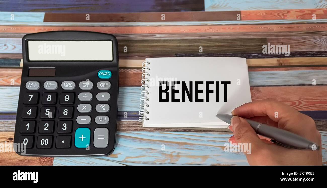 A woman's hand writes BENEFITS on a notepad, next to a calculator on a ...