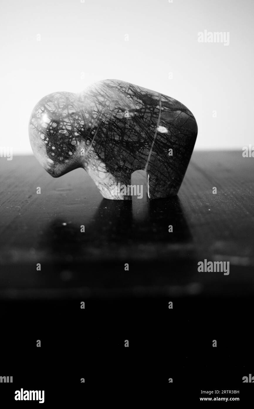 A stone statue of a bison standing tall on a shelf in a black and white ...