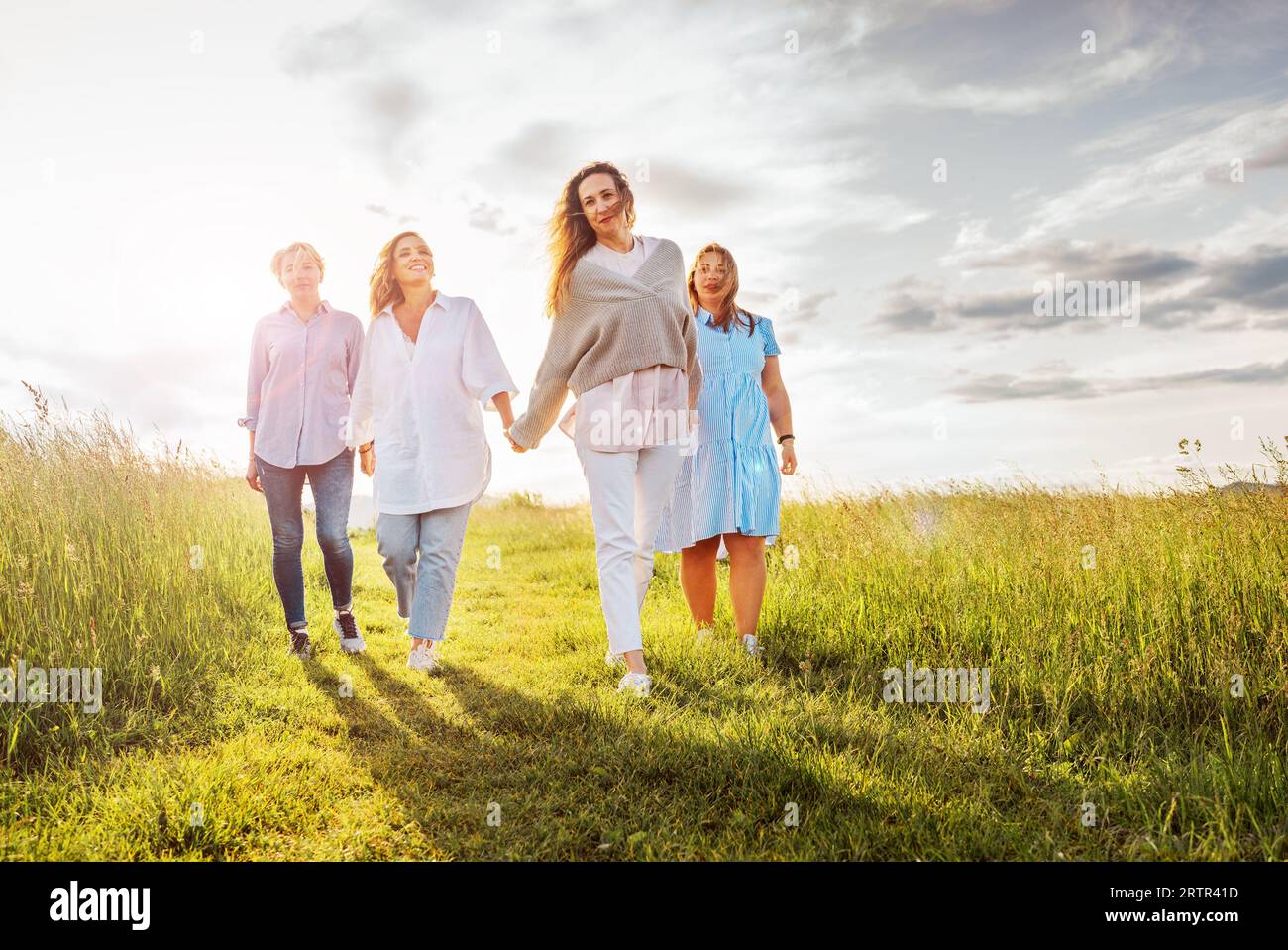 Portrait of four cheerful smiling women holding hand in hand walking by ...