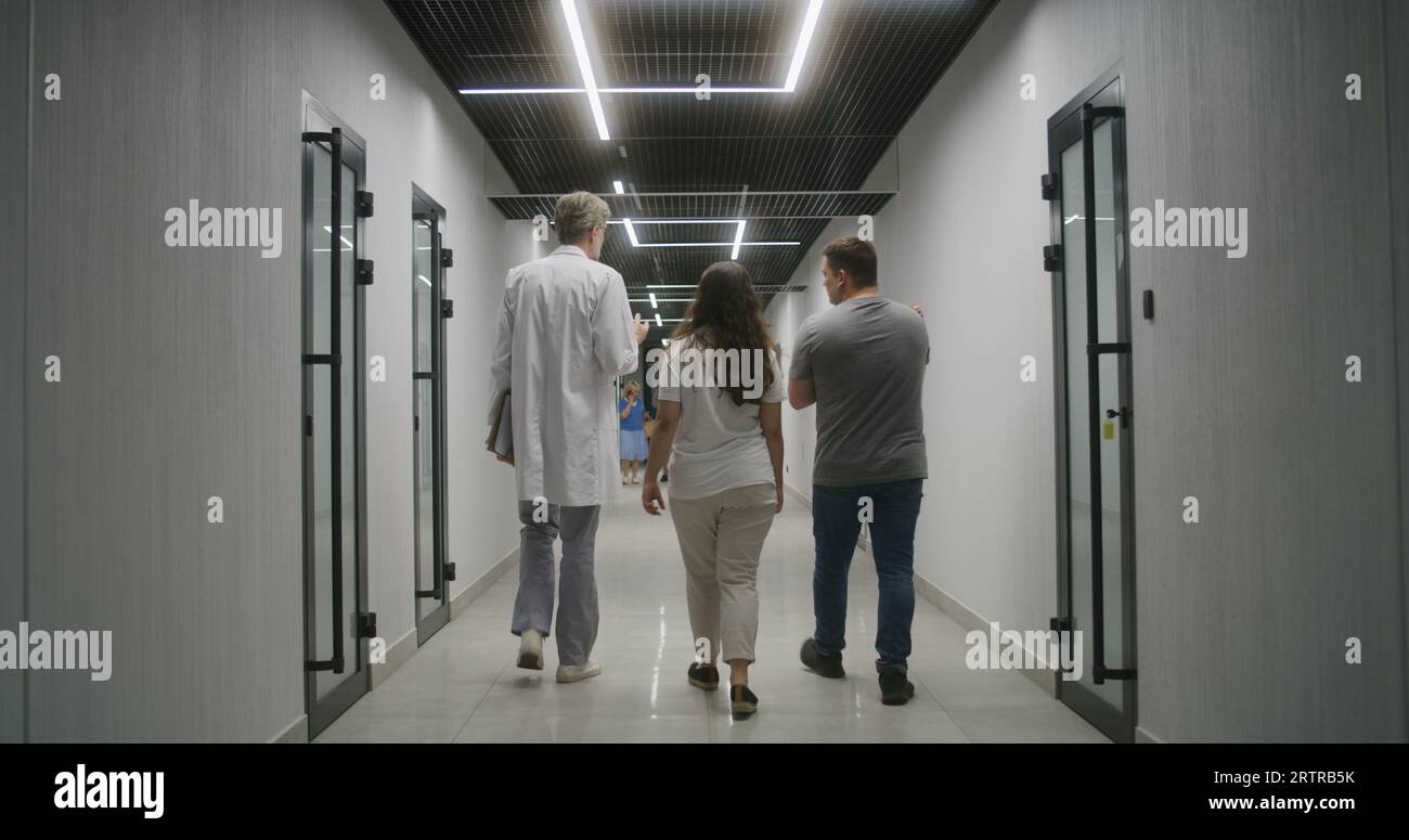 Doctor and family with child walk the clinic corridor. Doctor talks with patients, discusses ...