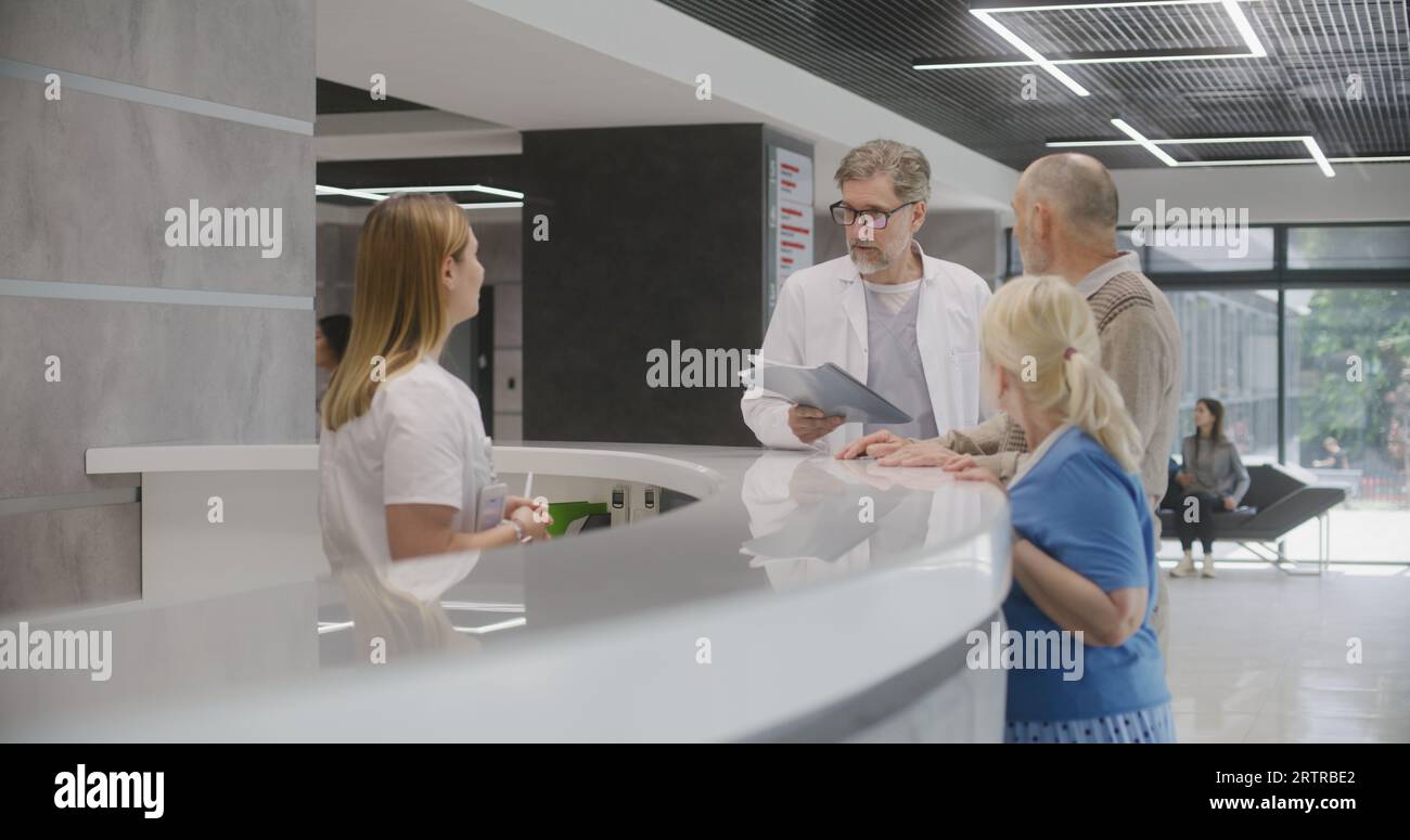 Elderly couple stand near reception desk in medical center lobby area ...