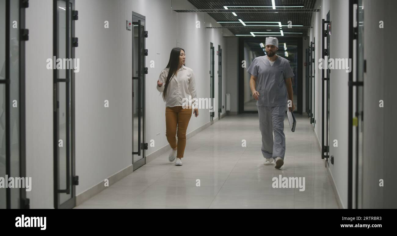 Medical worker, male nurse leads Asian woman along the clinic corridor ...
