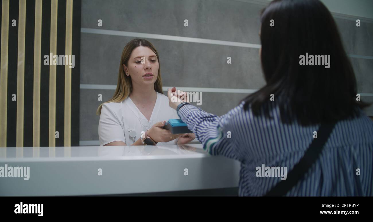 Female administrator stands at reception desk in clinic, gives terminal ...