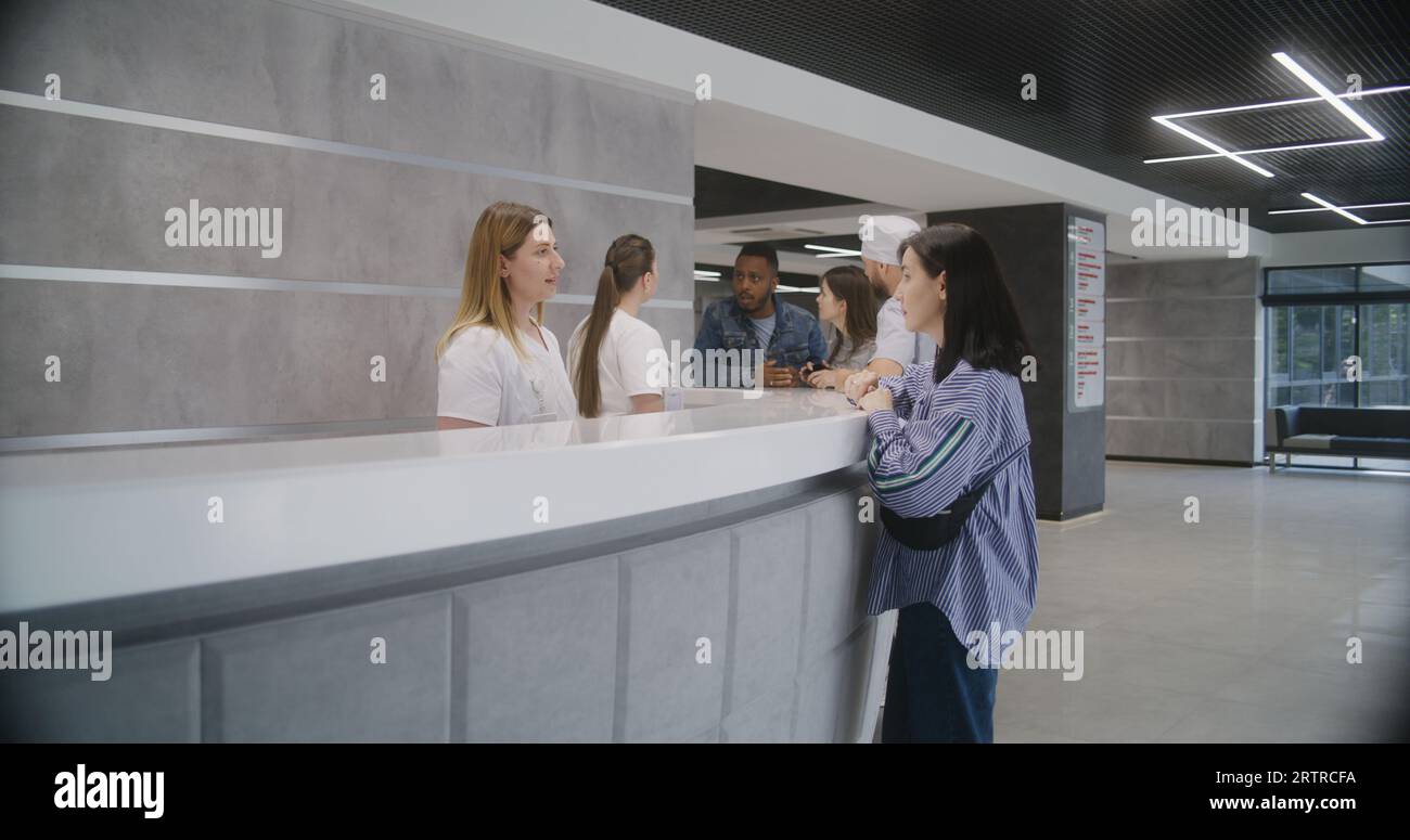 Adult woman stands at reception desk in clinic lobby entrance and makes ...