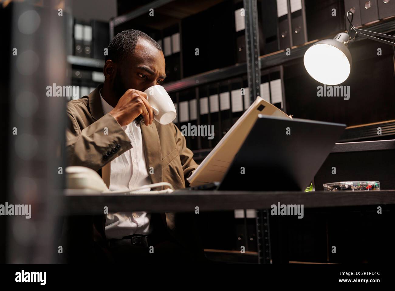 African american cop drinking coffee and reading csi report at night ...
